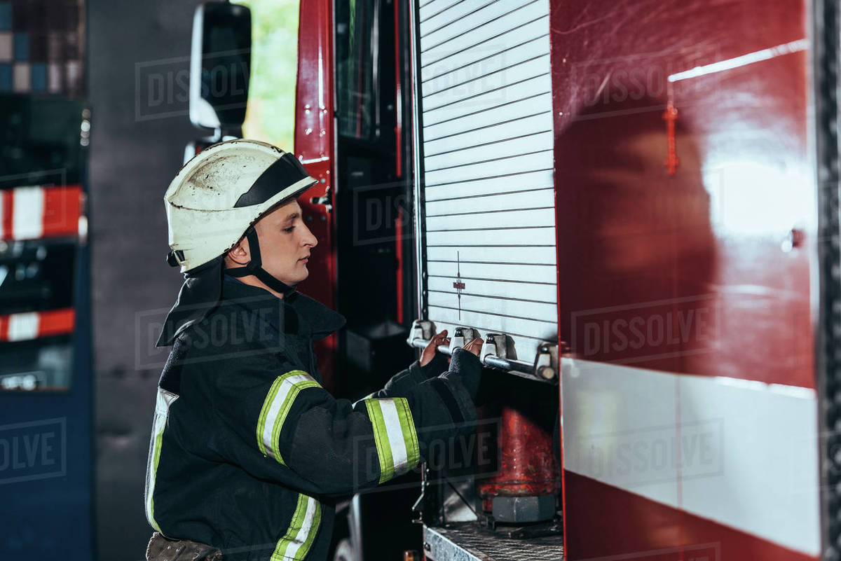 side view of fireman in uniform closing truck at fire department ...