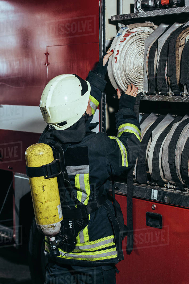 partial view of female firefighter with fire extinguisher on back ...