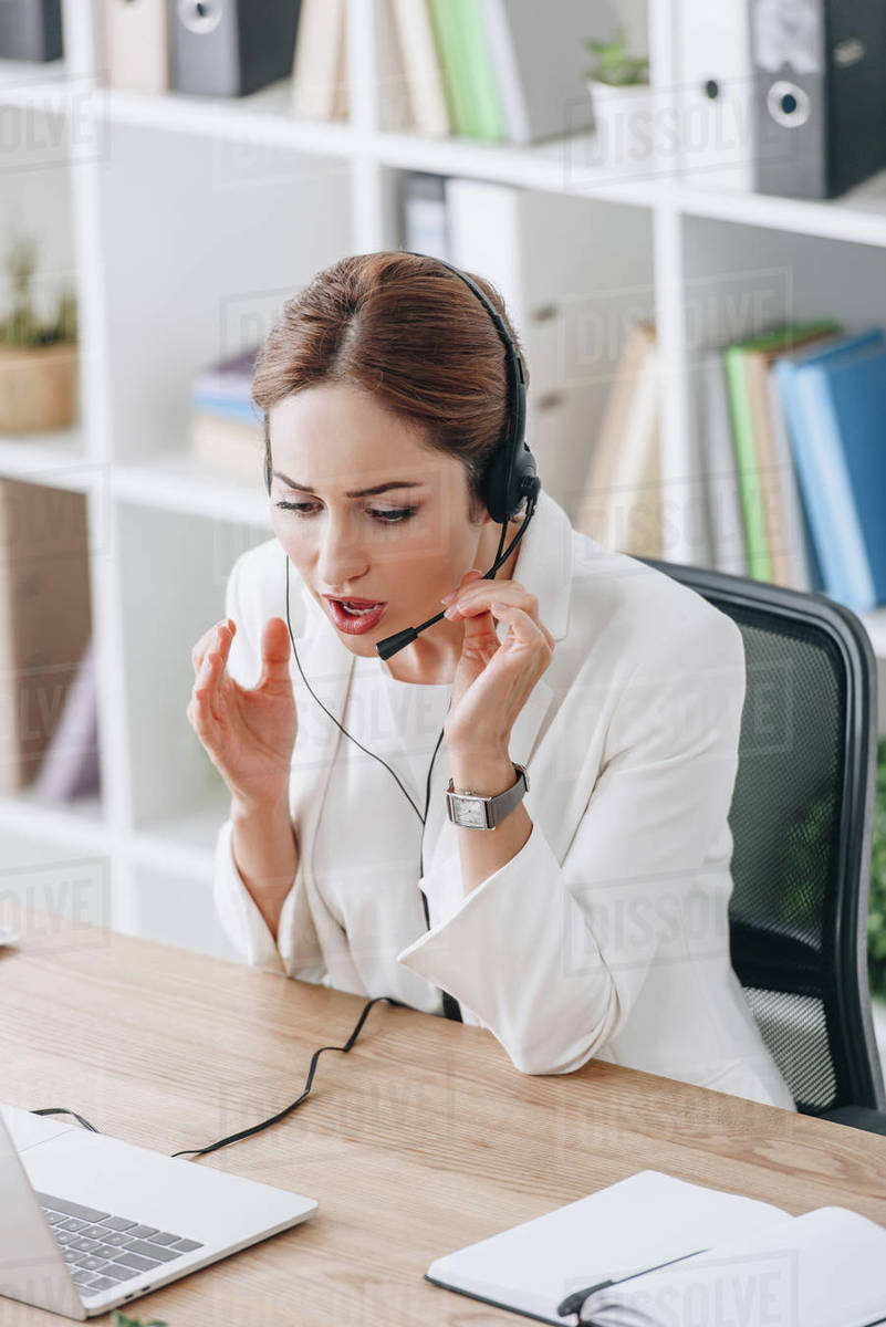 Worried operator working with headset and laptop in modern office ...