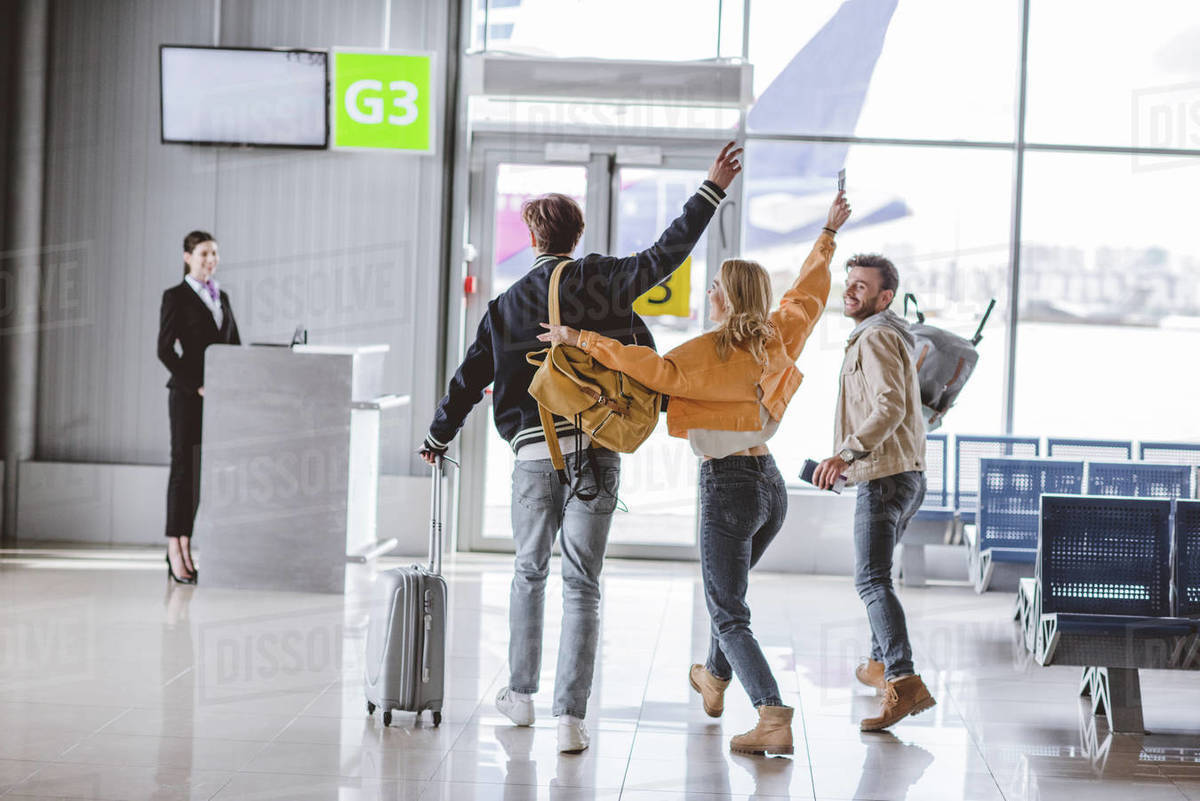 Back view of happy young friends waving hands and going to check-in ...