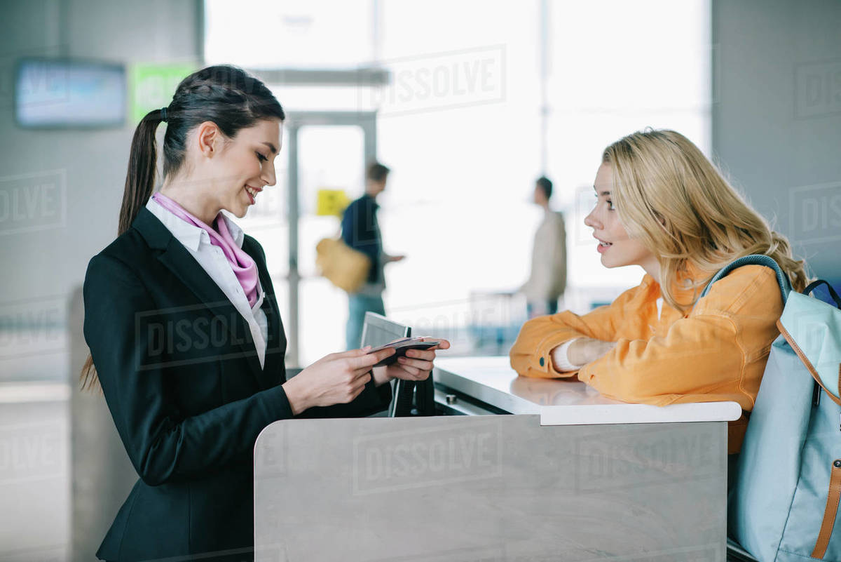 Side view of smiling airport worker checking documents of young female ...
