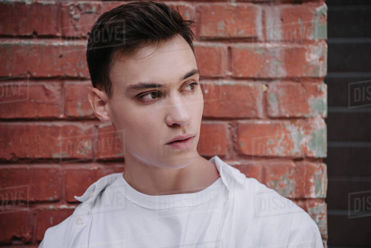 Portrait of handsome young man looking away near brick wall - Stock ...