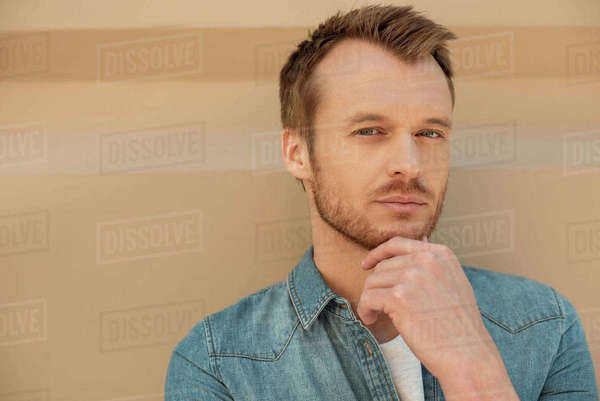 Close-up portrait of thoughtful young man looking at camera in front of ...