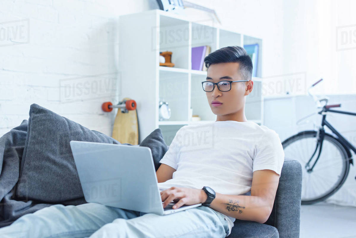 Handsome young Asian man using laptop on sofa at home - Royalty-free ...