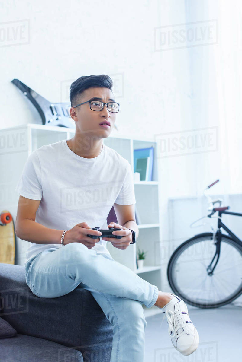 Upset handsome Asian man playing video game on sofa at home - Royalty ...