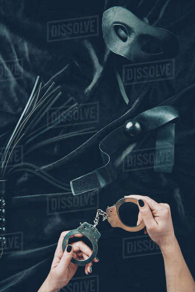 Cropped shot of woman holding handcuffs, leather whip, gag and mask on ...