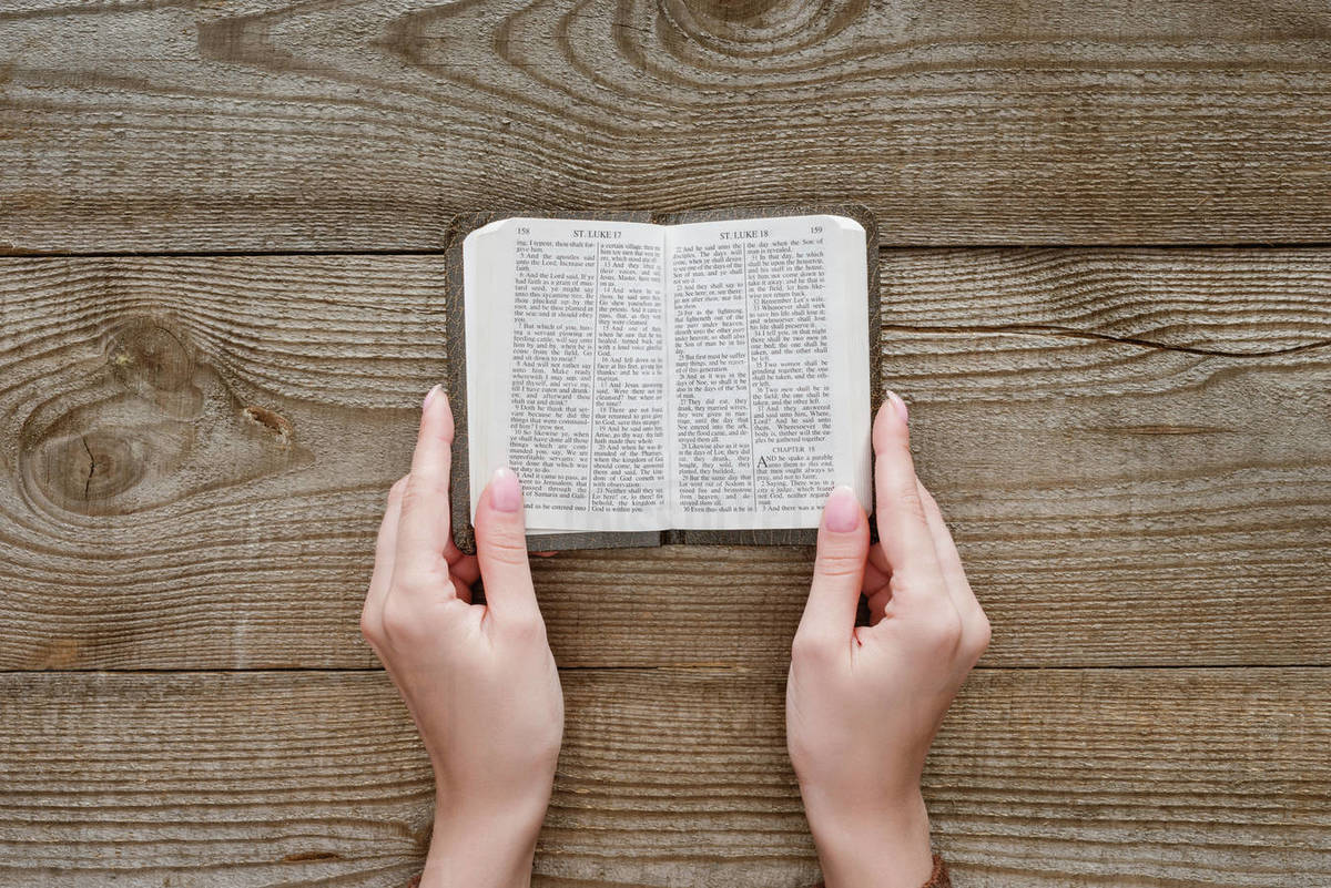 Cropped shot of woman holding miniature holy bible on wooden table ...