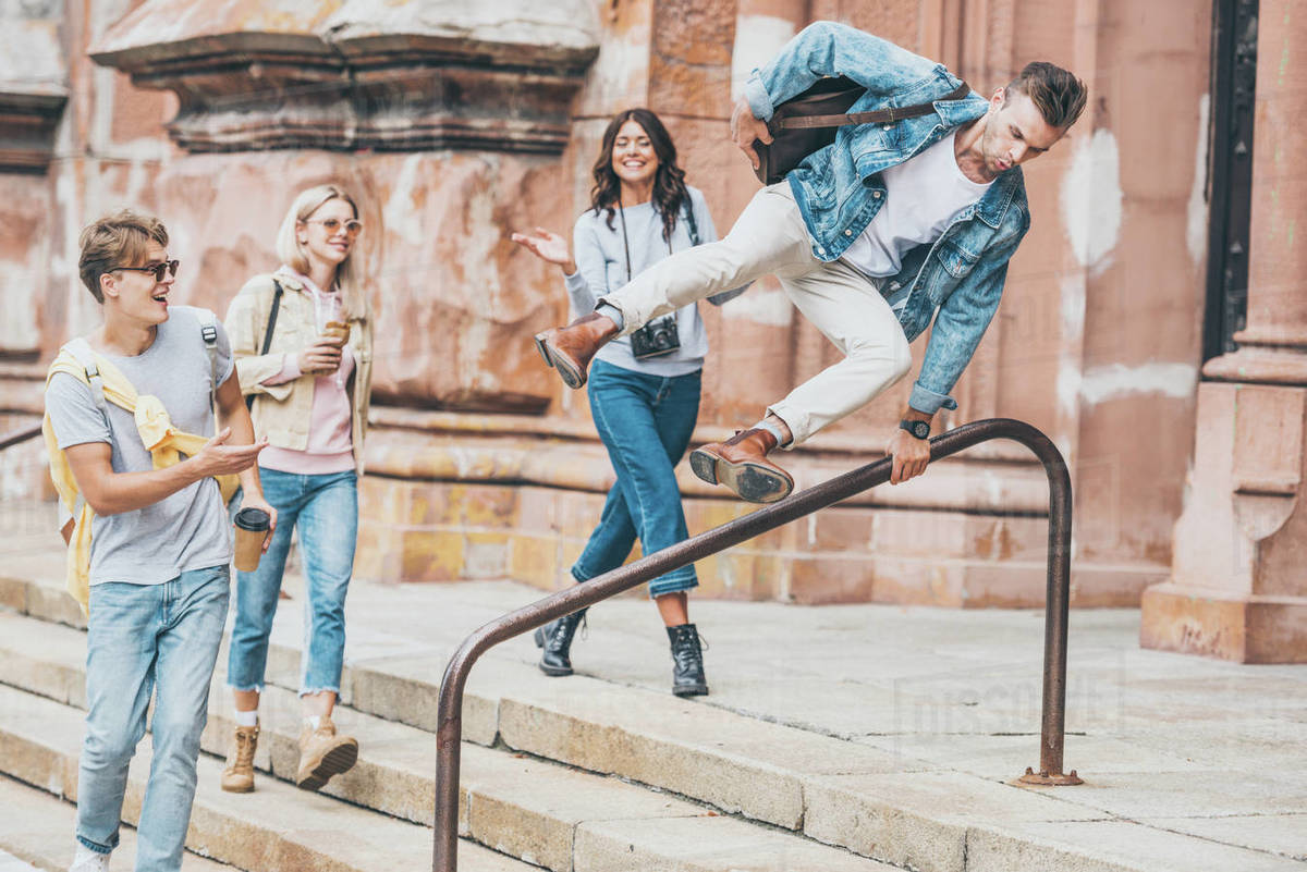 Young stylish friends walking in city while man jumping over railing ...