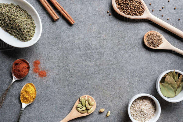 Various aromatic dried seasonings in bowls and spoons on grey ...