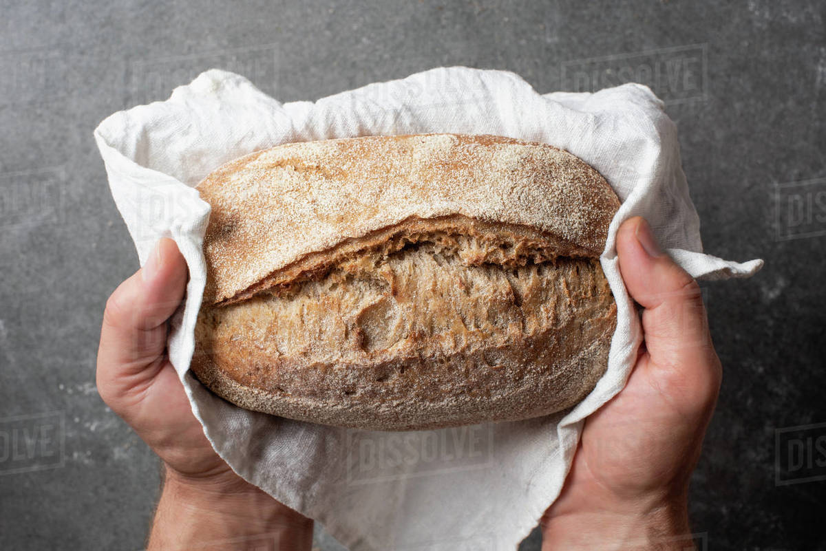 Cropped shot of man holding loaf of bread in hands on grey backdrop ...