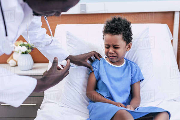 African American doctor making injection to little crying boy in clinic ...