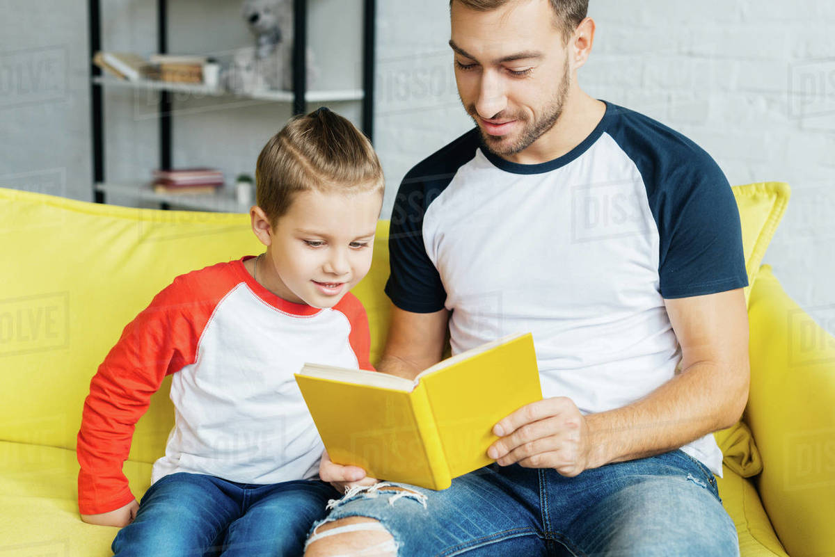 Portrait of father reading book for little son at home - Stock Photo ...