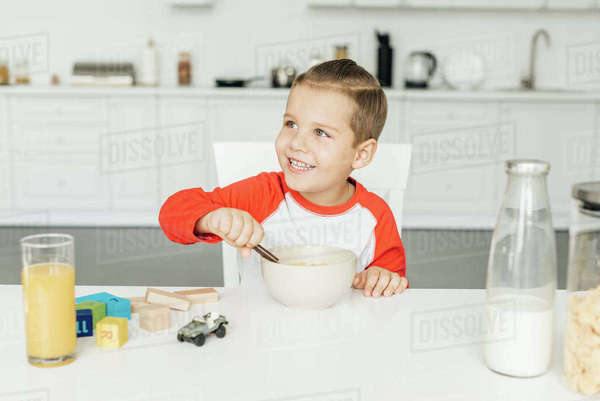 Portrait of little smiling boy having breakfast in kitchen at home ...