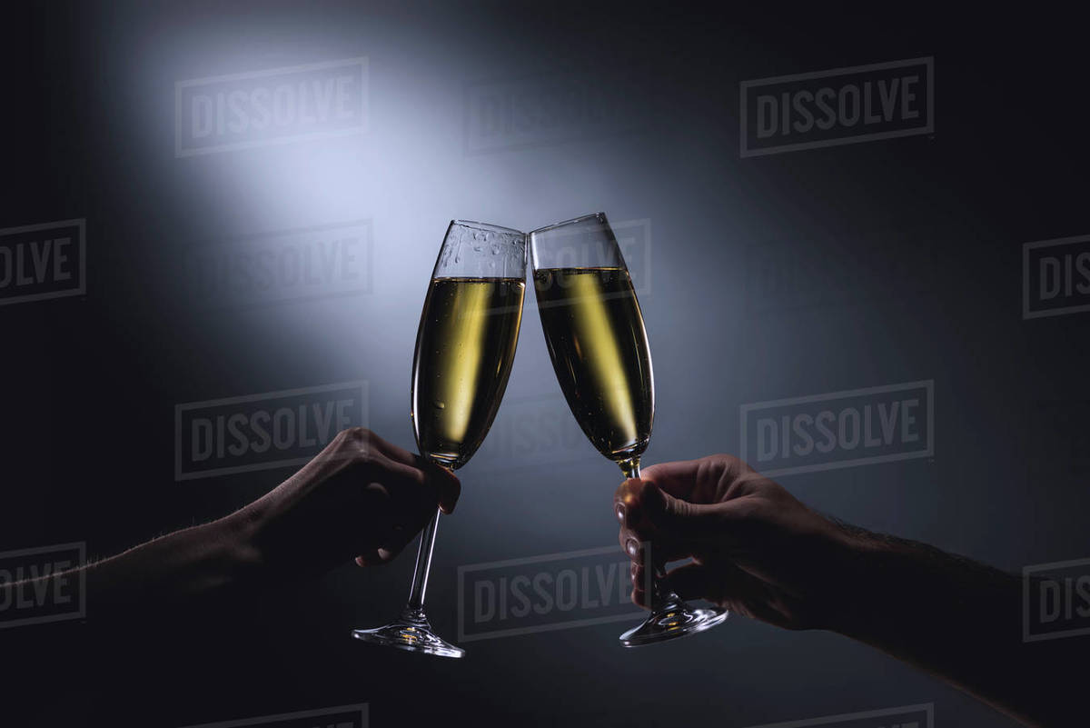 Cropped shot of couple clinking glasses of champagne on dark background ...