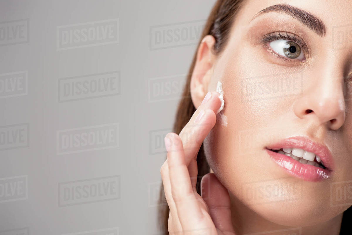 Beautiful woman applying face cream on perfect skin, isolated on grey ...