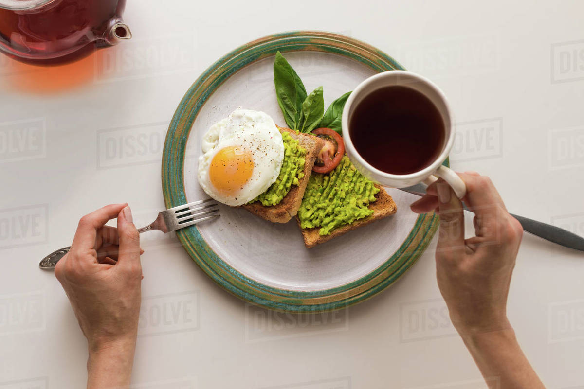 Cropped view of person eating fried egg and mashed avocado on toasts ...