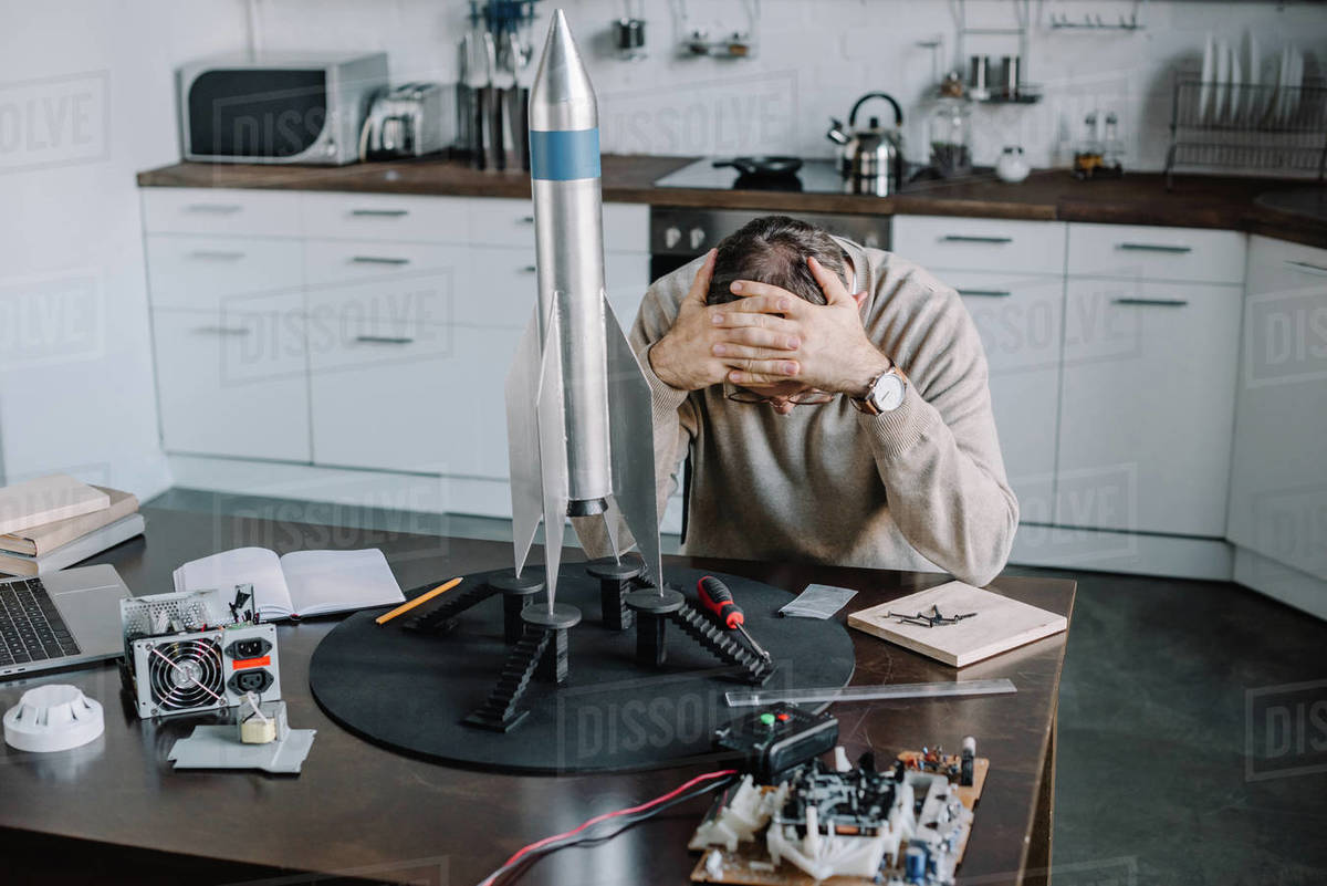 Exhausted engineer sitting at table with rocket model at home - Stock ...