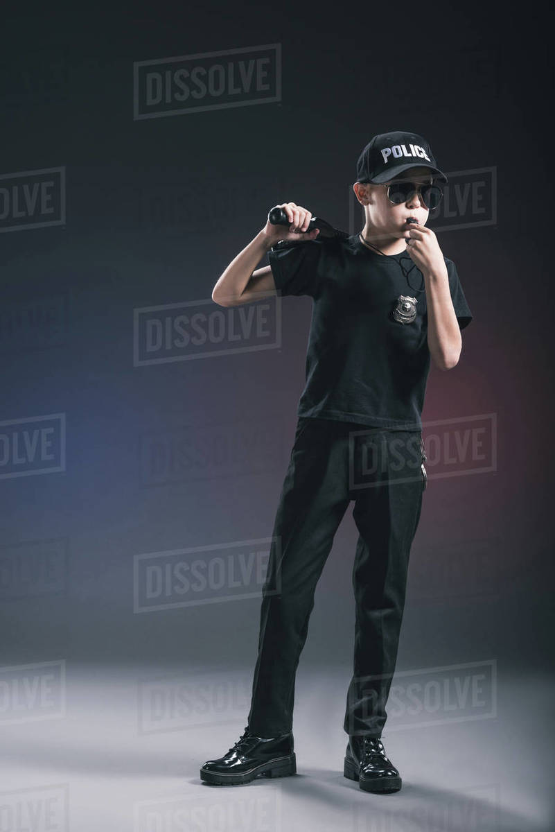 Boy in policeman uniform and sunglasses with whistle on dark background ...