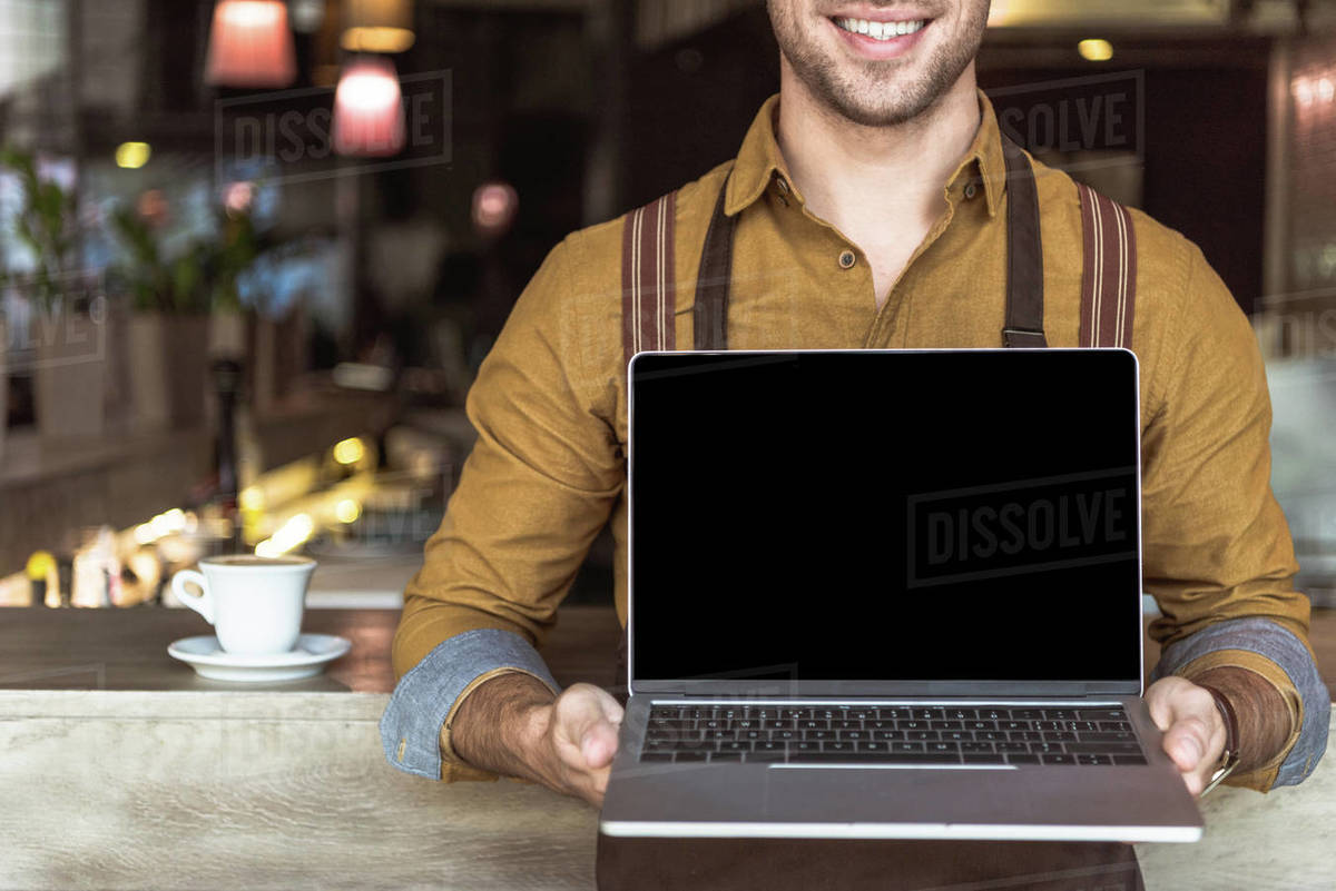 Happy young waiter holding laptop with blank screen in cafe - Stock ...