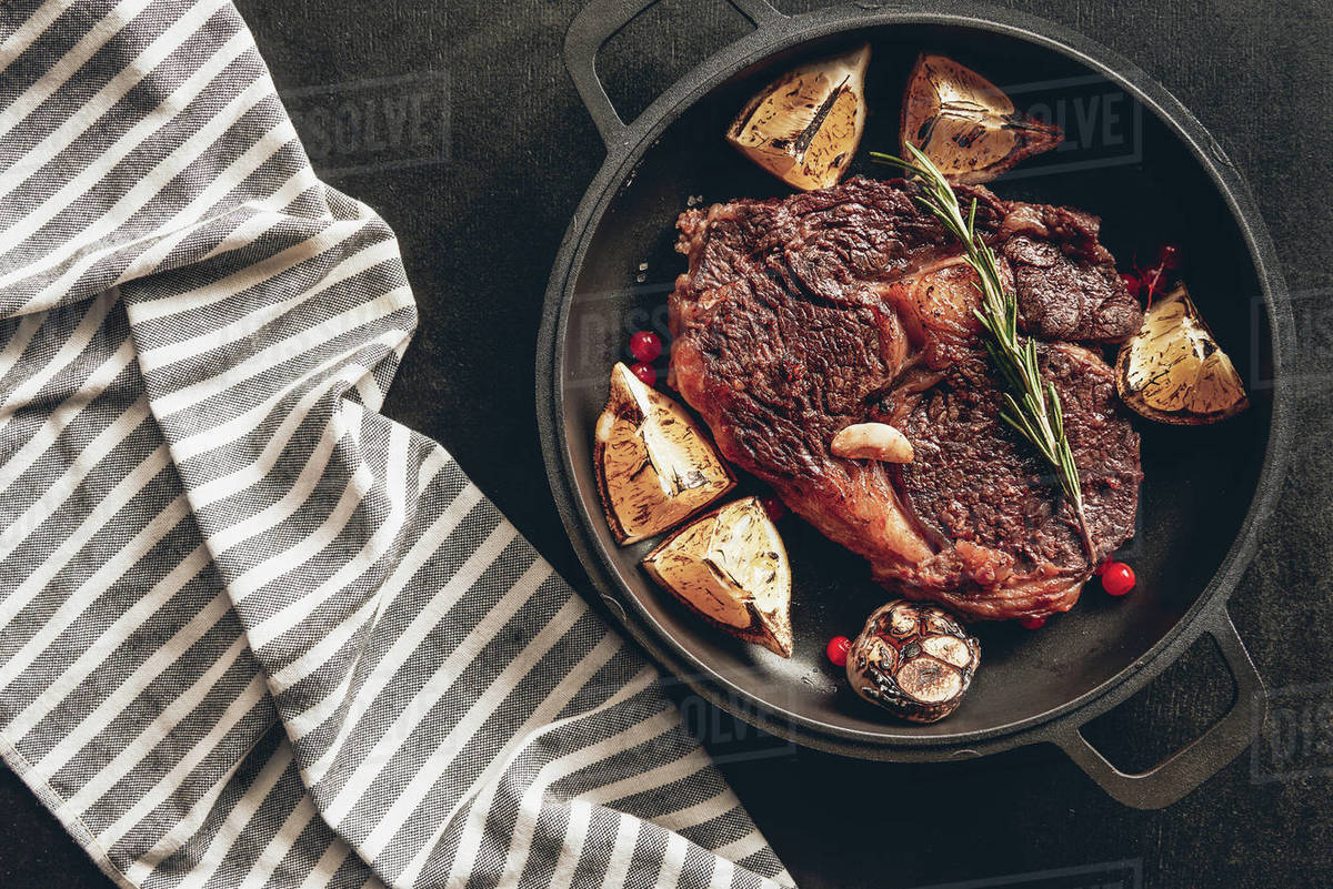 Top view of cooked steak with lemons and berries on frying pan ...