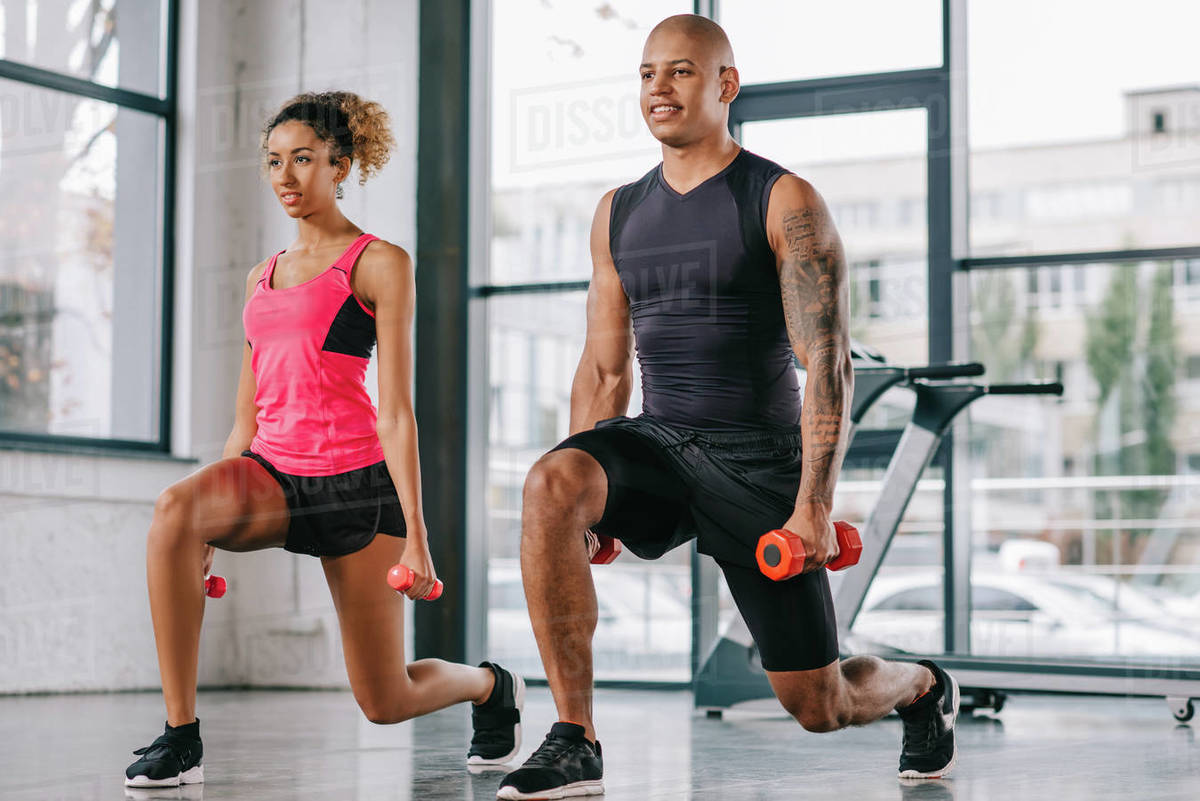 Cheerful couple of athletes doing exercise with dumbbells at gym ...
