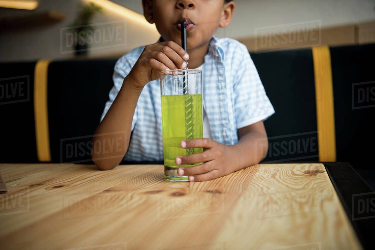 Cropped shot of cute African American child drinking lemonade in cafe ...