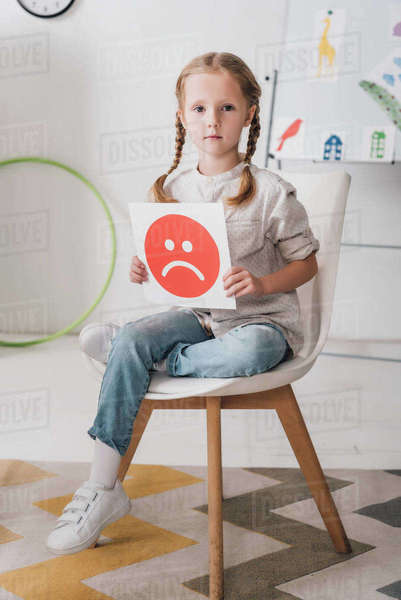 Lonely little child sitting on chair holding sad face symbol - Stock ...