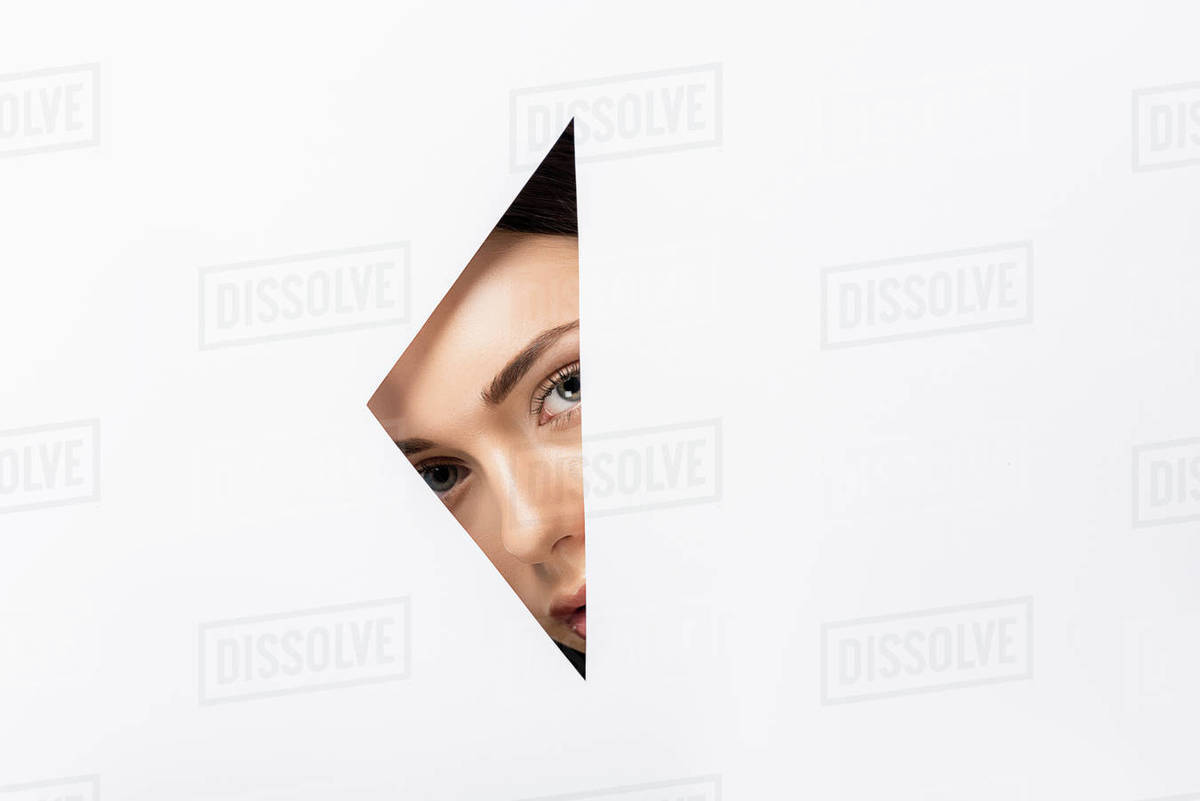 beautiful young woman looking at camera through hole on white - Royalty ...