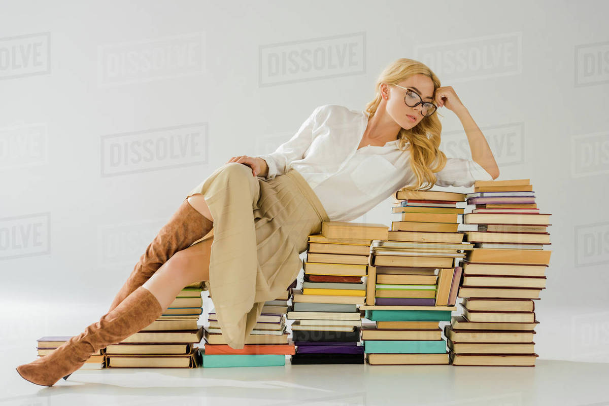 beautiful blonde woman in glasses laying on pile of retro books ...