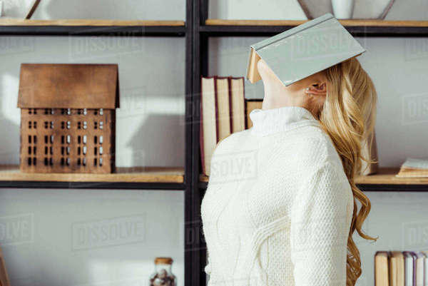blonde woman putting book on face near rack - Royalty-free Stock Photo ...