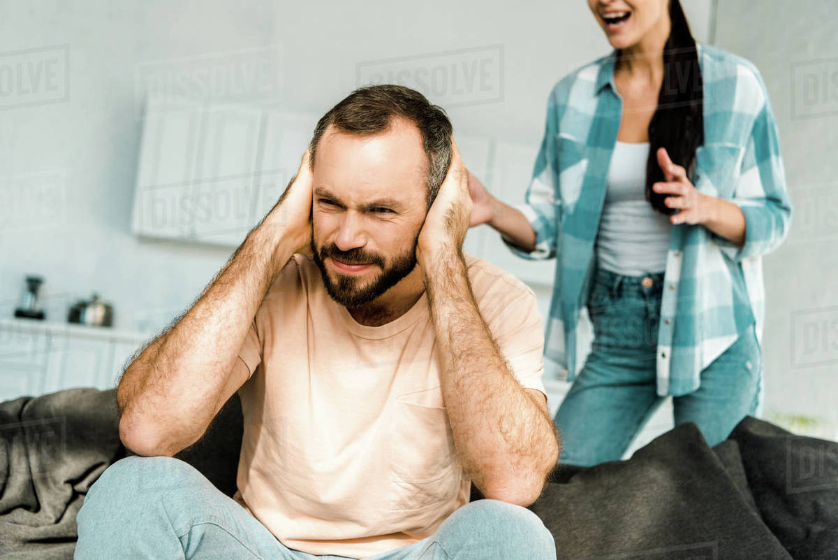 Frustrated husband on foreground covering ears with hands and having ...