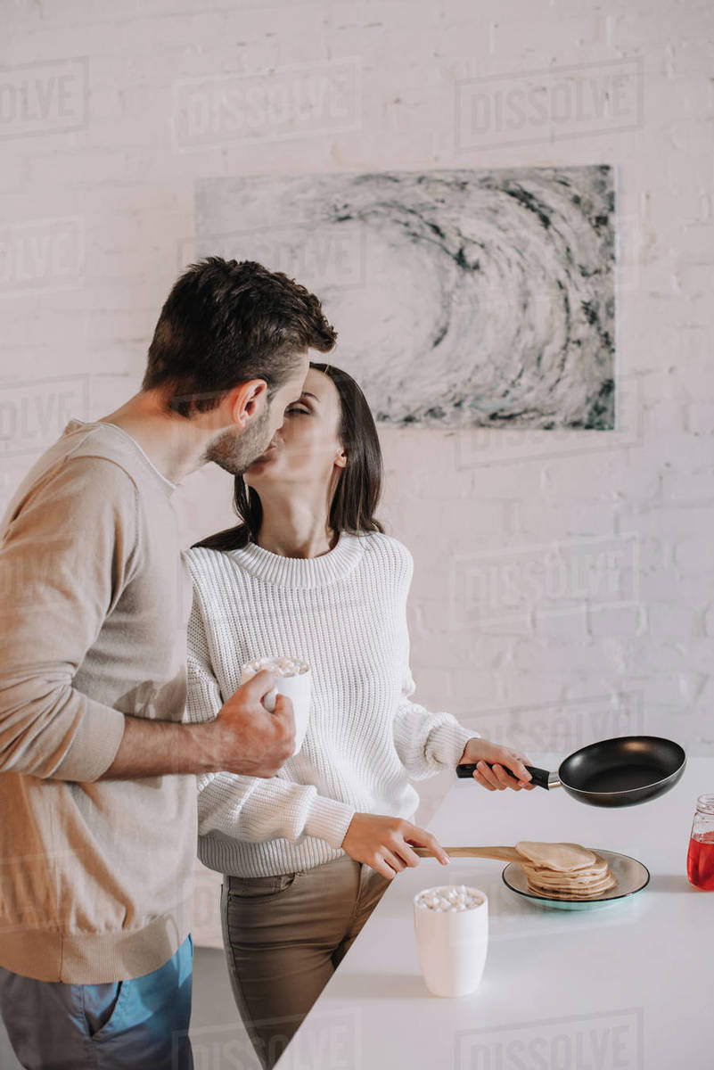 Beautiful young couple making breakfast together and kissing - Royalty ...