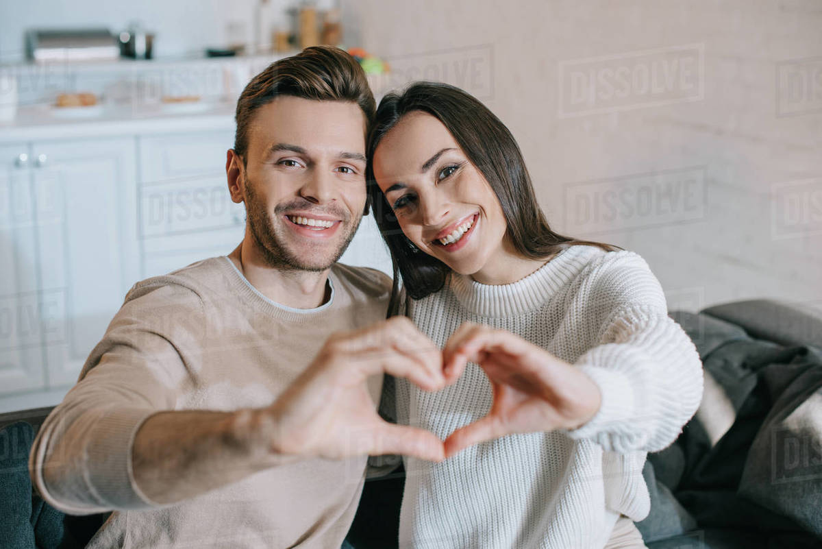 Beautiful young couple making heart symbol with hands and looking at ...