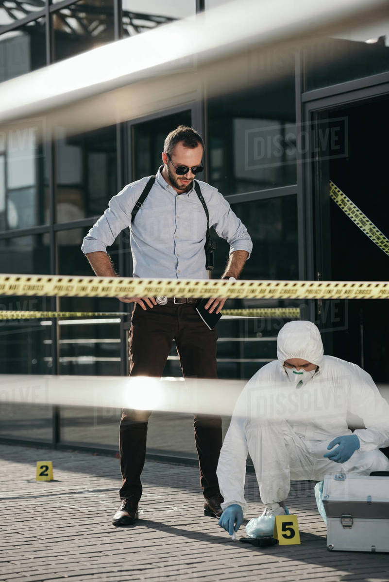 Male detective looking at work of criminologist - Stock Photo - Dissolve