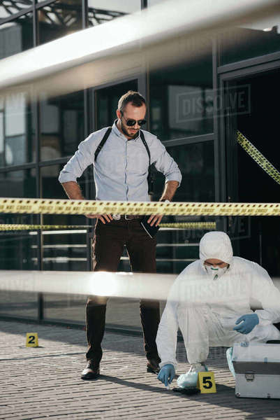 Male detective looking at work of criminologist - Stock Photo - Dissolve