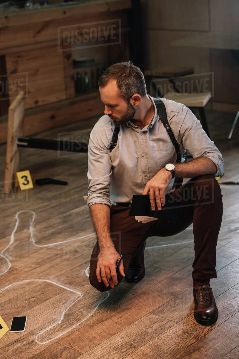 Serious male detective sitting at crime scene and looking on chalk line ...