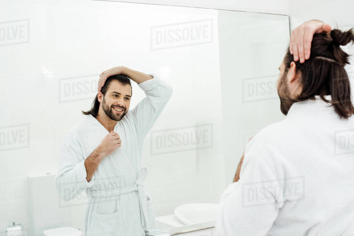 Handsome man looking in mirror and smiling in white bathroom - Royalty ...