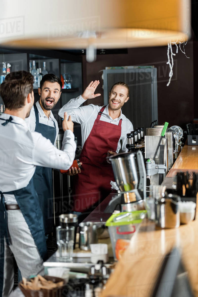 Cheerful barmen in aprons high five at workplace - Stock Photo - Dissolve