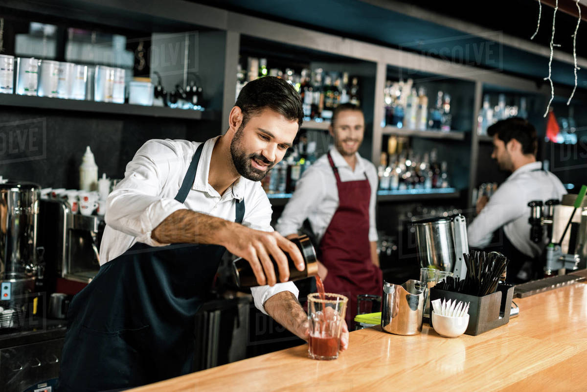 Smiling bartender pouring cocktail in glass at wooden counter - Stock ...