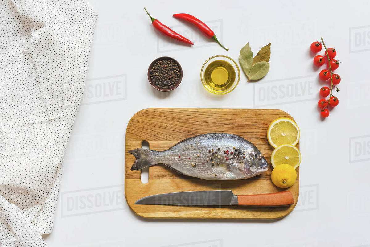 elevated view of uncooked fish and various ingredients on white table ...