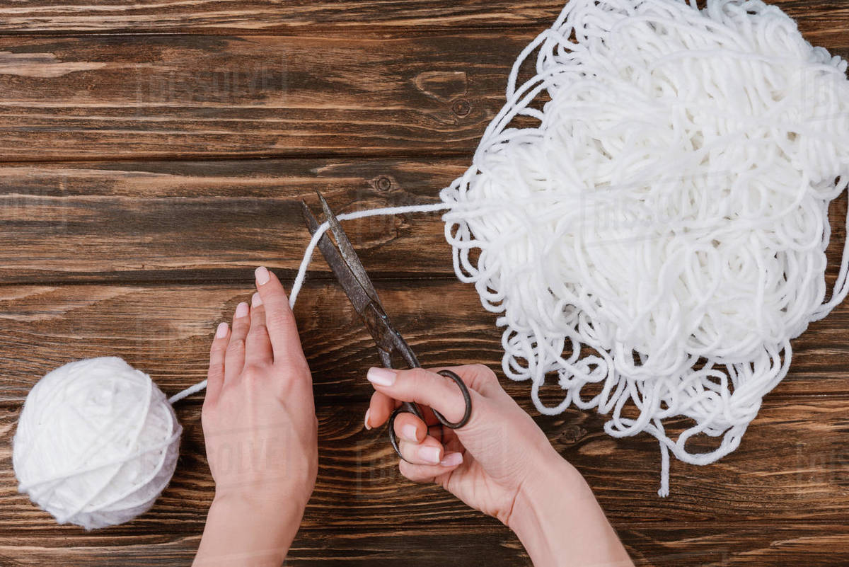 partial view of woman cutting white knitting thread with scissors on ...