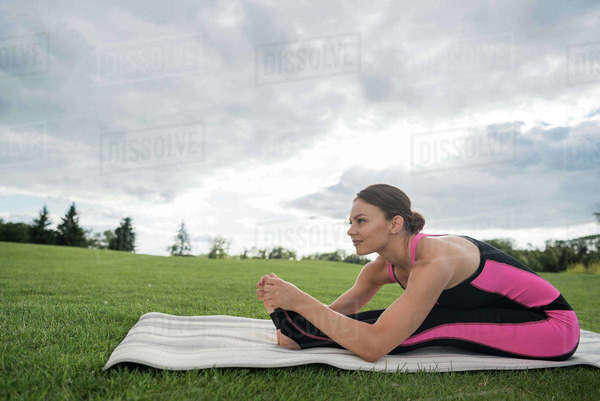 Side view of smiling woman practicing seated forward bend yoga pose at ...