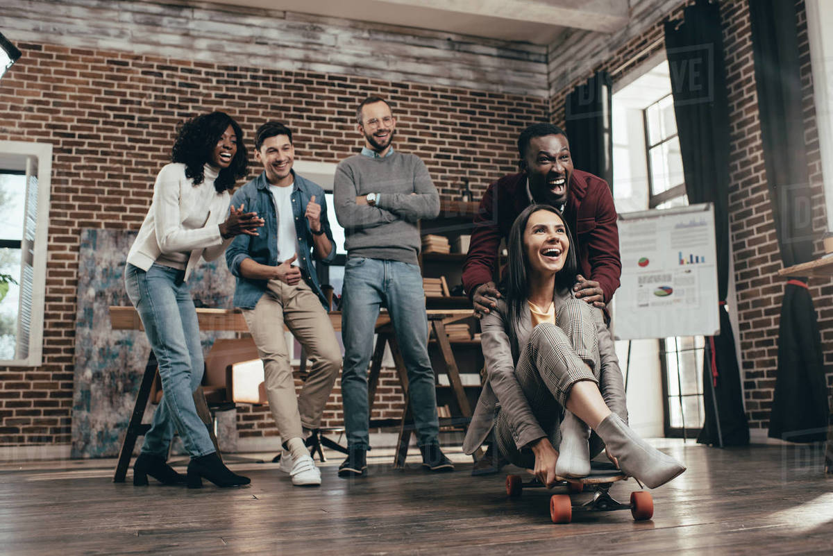 Cheerful group of multiethnic coworkers having fun with skateboard in ...