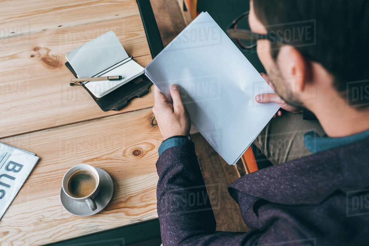 back view of businessman looking at blank papers in hands in cafe ...