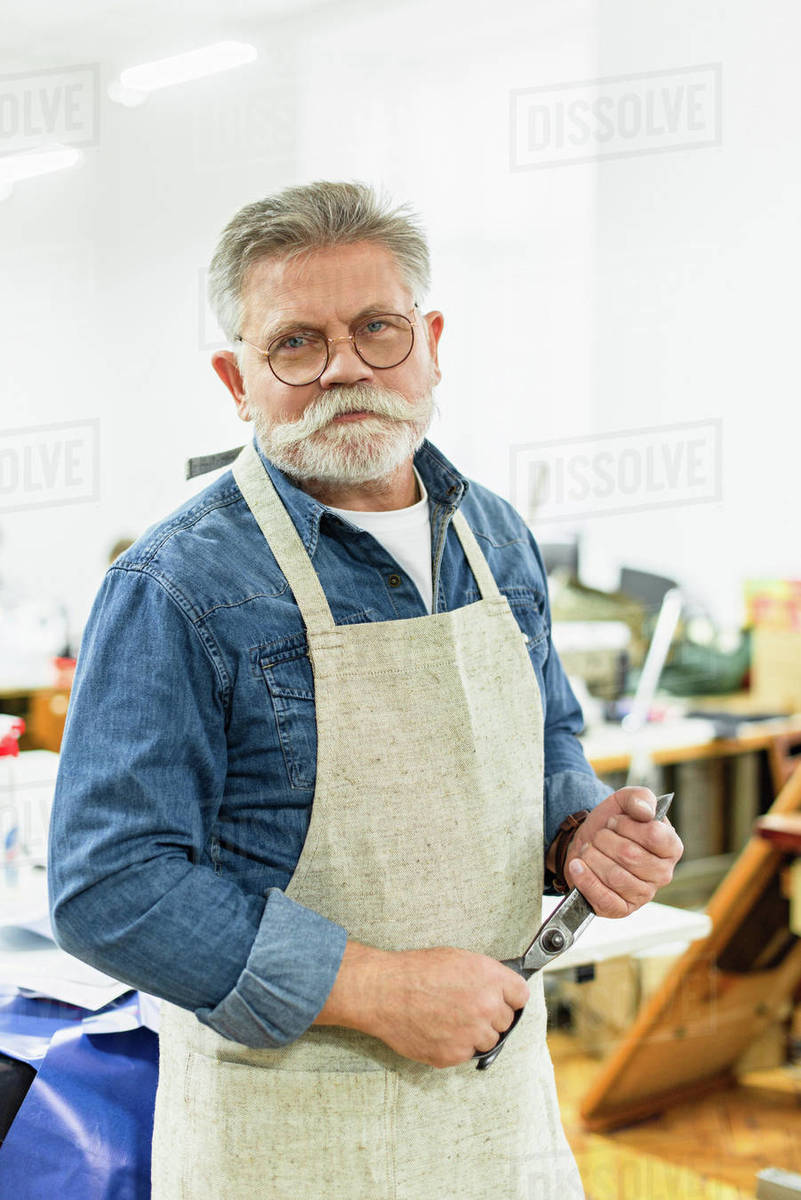 smiling middle aged male craftsman in apron posing with scissors at ...