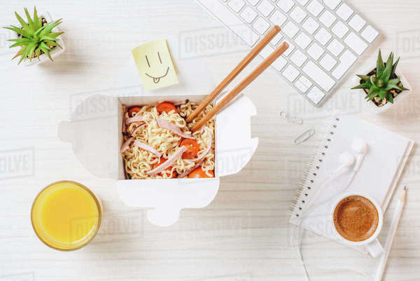 Elevated view of wok box with chopsticks, orange juice, symbol of smile ...
