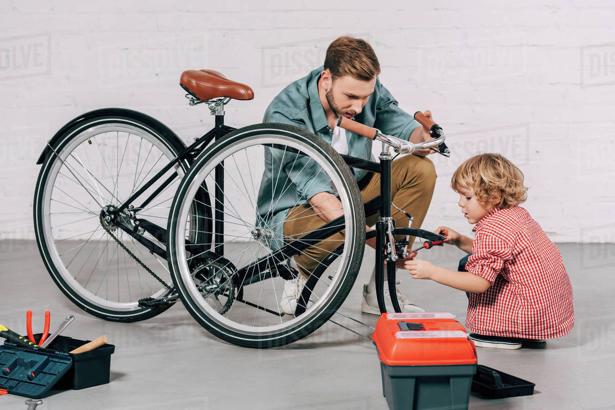 Man helping little boy fixing bicycle near tools box in workshop ...