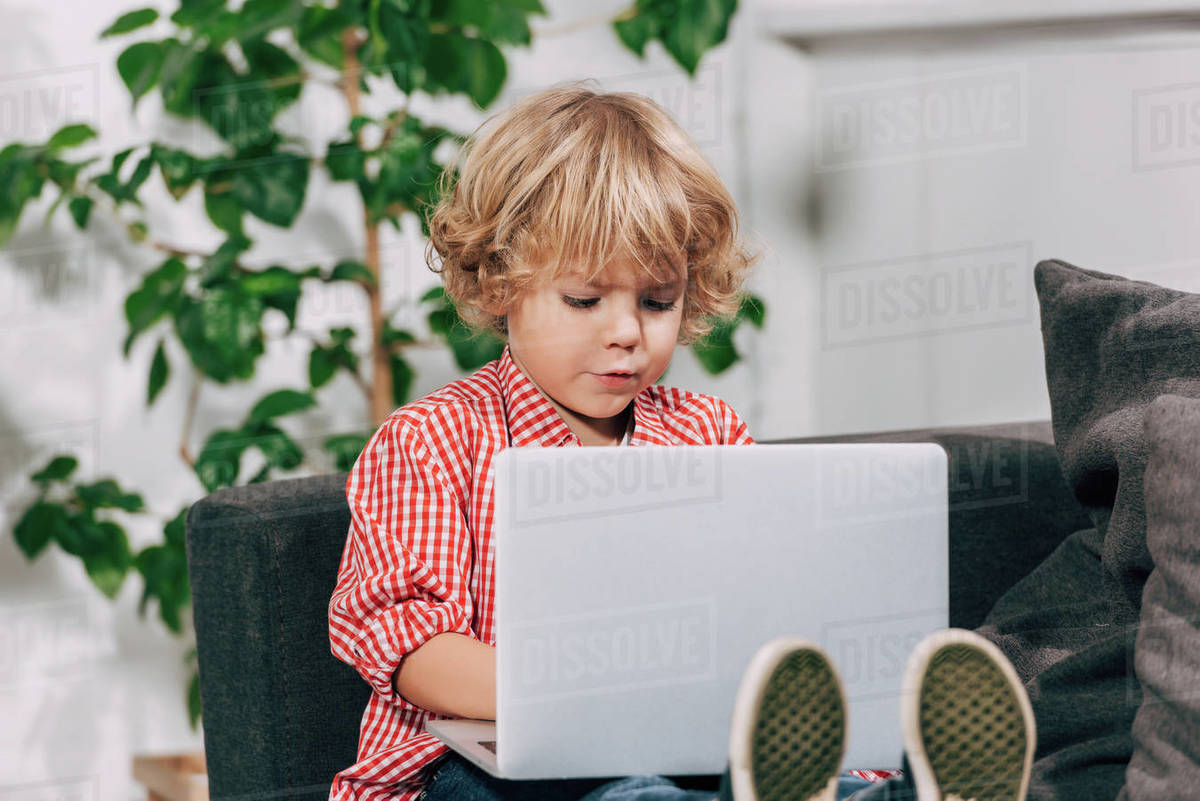 Focused little kid using laptop on sofa at home - Royalty-free Stock ...