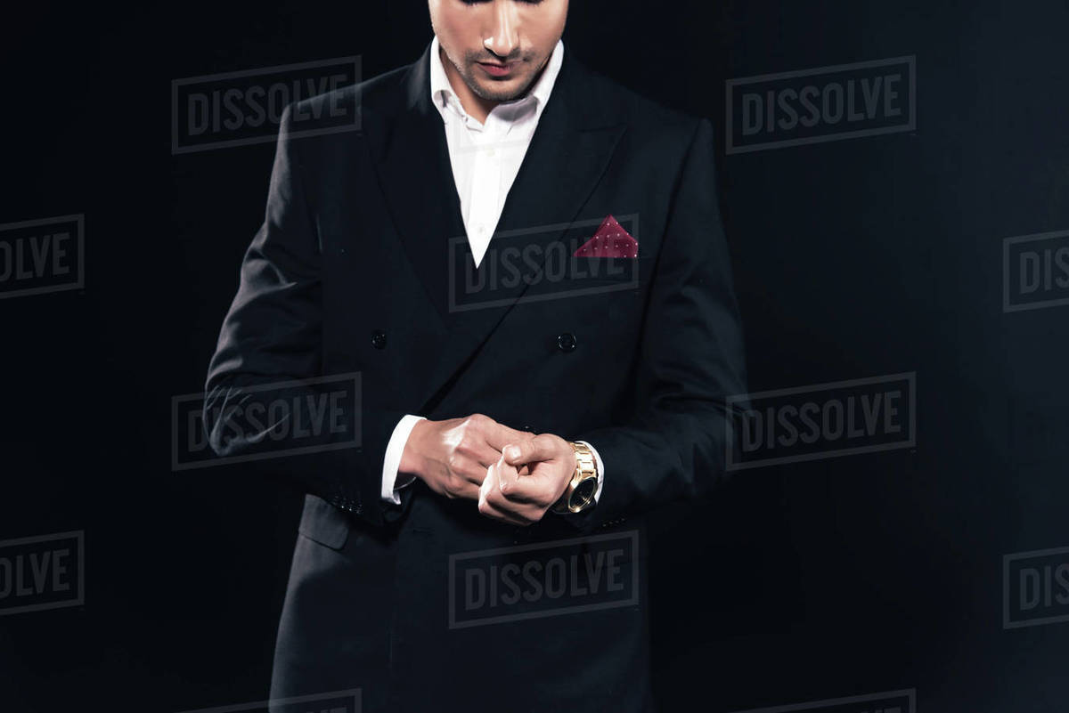 Cropped view of man in suit putting on watch isolated on black ...