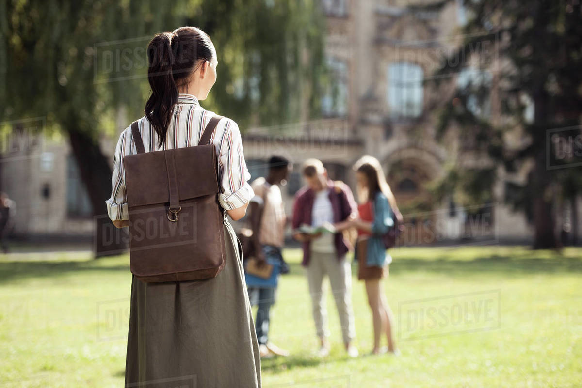 Back view of young female student with backpack looking at classmates ...